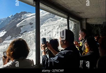 Tourists look through a glass window at the icefalls of the Eiger ...
