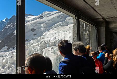 Tourists look through a glass window at the icefalls of the Eiger ...