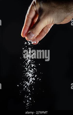 Male hand sprinkling edible salt at black background Stock Photo - Alamy