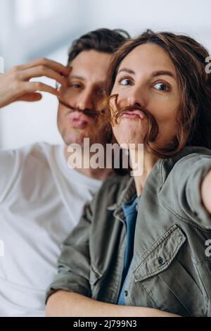 Happy newlyweds play and pose making mustaches with curly brunette hair ...