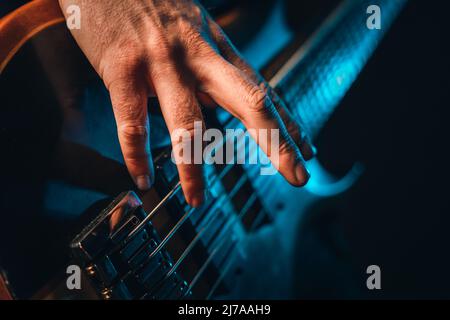 Closeup of male fingers playing five stringed electric bass guitar ...