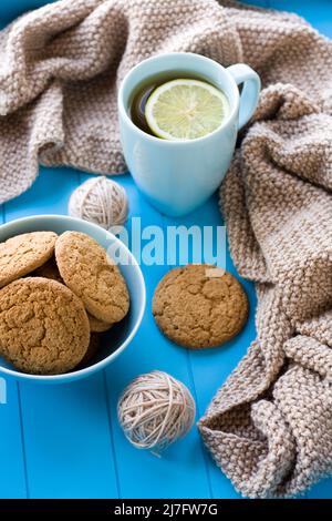 A cup of tea with lemon, biscuits, beige knitted blanket lie on blue ...