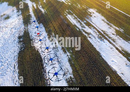 Many agrodrones are on the green field. The snow has not melted yet ...