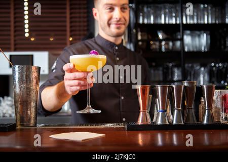 Crop friendly young male barkeeper in uniform serving delicious sour ...