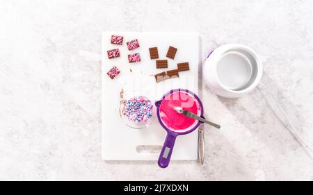 Flat lay. Drizzling melted pink chocolate on top of the mini chocolates ...