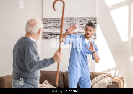 Aggressive pensioner brandishing the walking stick at his caretaker ...