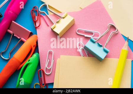 top view of fold back clips near paper notes and colorful pens on pink ...