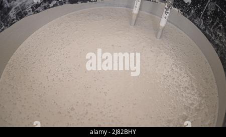 A worker using a mixer mixes the self-leveling floor in a bucket. Stir ...