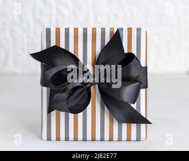 Gift box wrapped in Striped geometric paper with black ribbon bow close ...