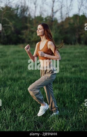 An athletic woman jogs on the grass in green pants and sneakers and ...