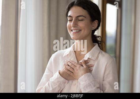 Grateful young woman put folded palms on chest posing indoor Stock ...
