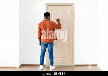 Rear View Of Black Guy Knocking At Entry Door Indoors Stock Photo - Alamy