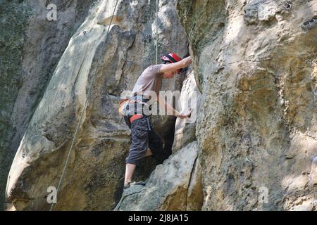 Determined climber clambering up steep wall of rocky mountain ...
