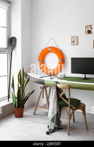 Stylish workplace with modern computer and SUP board near light wall in ...