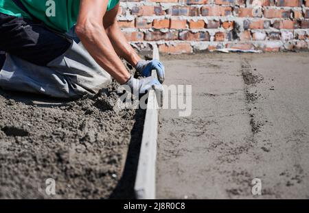 Man builder placing screed rail on the floor covered with sand-cement ...