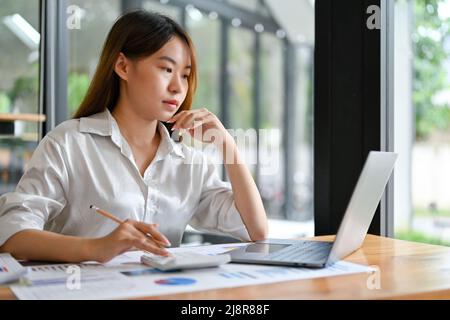 Concentrated Asian female financial analysts or businesswoman reviewing ...