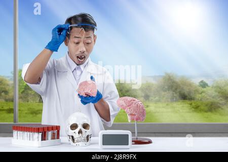 Asian nerd scientist standing and holding a skull head with a ...