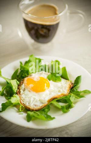 one fried egg with arugula and lettuce in a plate on a wooden table ...