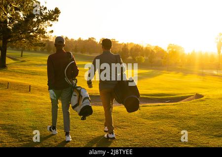 Rear view of young male multiracial friends with golf bags walking ...