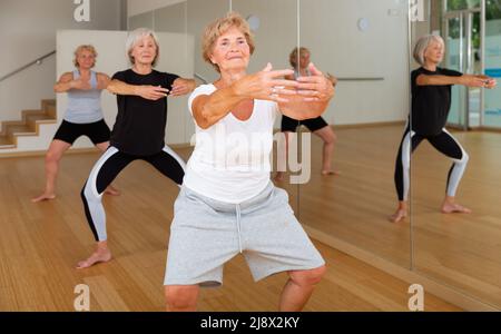 Mature women perform a plie squat while in the position of a ballet ...