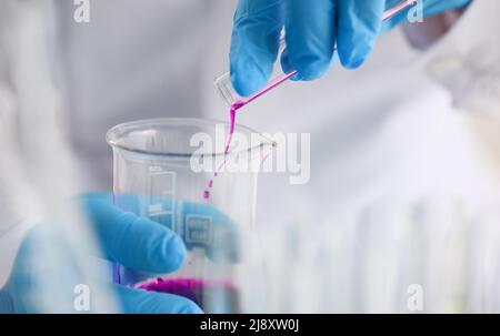 Scientist pour pink liquid from flask in medical chemistry laboratory ...