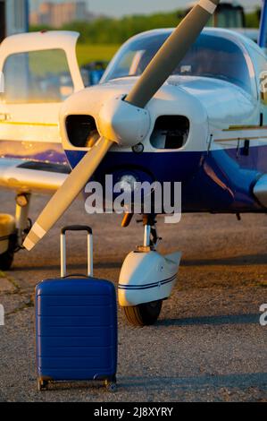 A blue suitcase and a parked small private jet. Quadruple plane with a ...