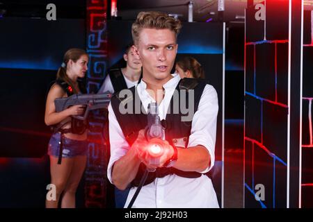 Emotional guy with laser pistol playing laser tag with friends on dark ...