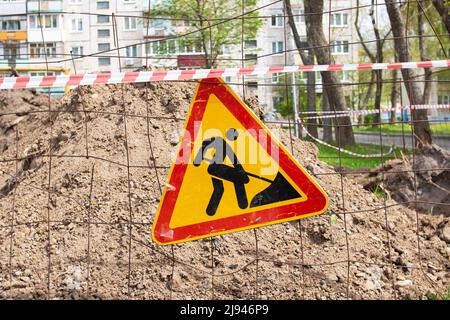 Roadworks, under construction. Earthwork sign on fence with trench hole ...