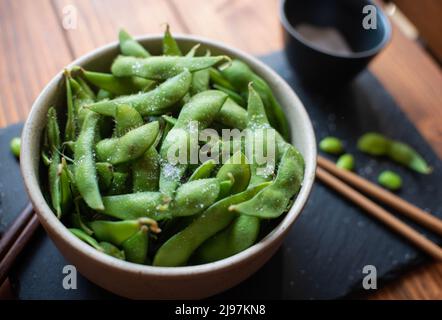 Close-up of steamed edamame sprinkled with sea salt on a dark stone ...
