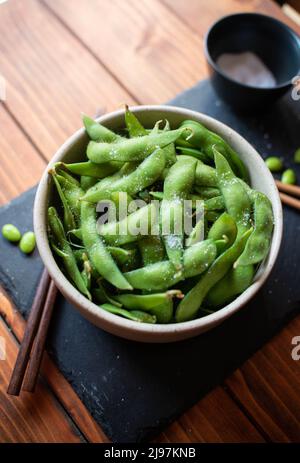 Close-up of steamed edamame sprinkled with sea salt on a dark stone ...