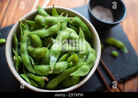 Close-up of steamed edamame sprinkled with sea salt on a dark stone ...