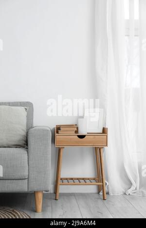 Table with frame, books and sofa near light wall Stock Photo - Alamy
