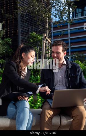 Two asian business coworkers outside office buildings discuss and ...