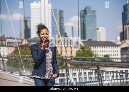 Smiling businesswoman sending voicemail through smart phone at rooftop ...
