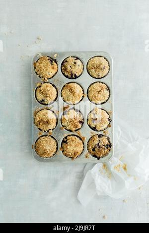 Baking tray with muffins, whisk and scattered flour on lilac background ...