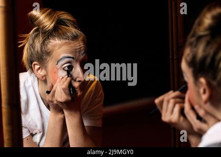 Young professional female mime in casual clothes painting the eyebrows ...