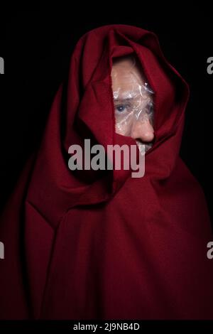 Man covered in red cloth with plastic on his face against black ...