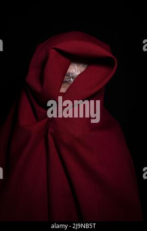 Man covered in red cloth with plastic on his face against black ...