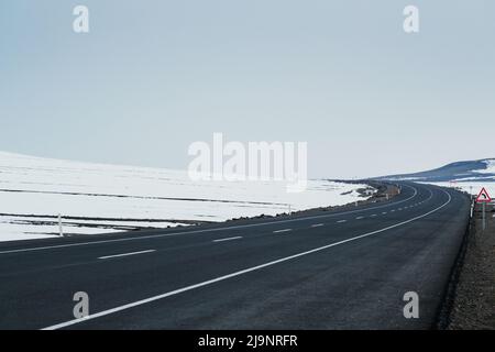 Diagonal view of an emtpy asphalt road with lanes and snow in winter ...