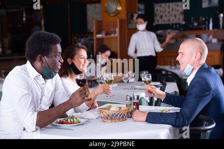 Cheerful people in masks having dinner in restaurant Stock Photo - Alamy