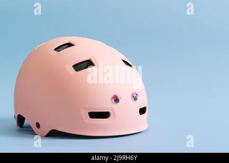 Pink helmet with funny doll eyes on blue background. Childs outdoors ...