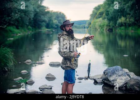 Fisherman fishing on a rever. Relaxed fisher man with a fishing rod on ...