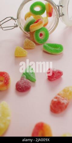 Vertical image of jelly candy spilling out of glass jar on pink ...