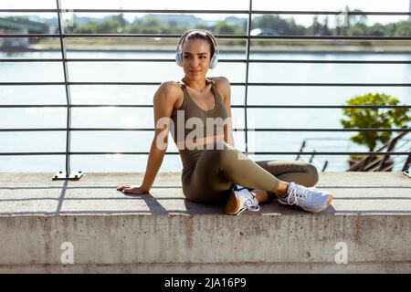 Pretty young woman with earphones takes a break after running in the ...