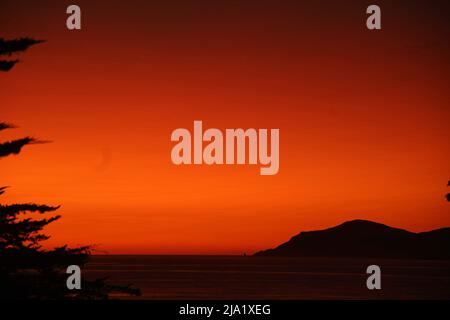 Fiery red sunset silouetting trees and island Stock Photo - Alamy