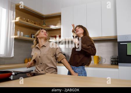 Playful woman dancing with wooden spatula while cooking in home kitchen ...