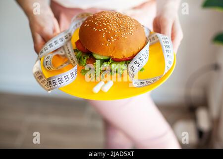 Woman holding harmful fat burger with measuring tape Stock Photo - Alamy