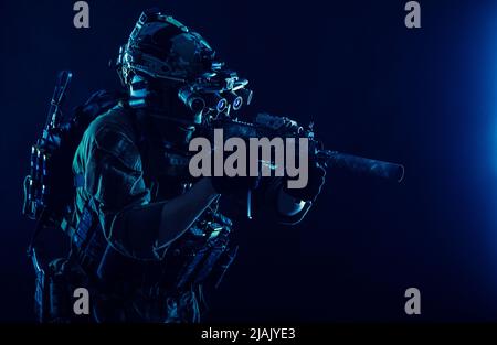 A special operations soldier wearing night vision device, aiming short ...
