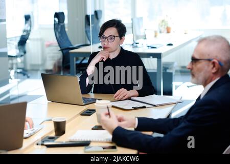 Pensive serious young businesswoman sitting at cafe table, drinking ...