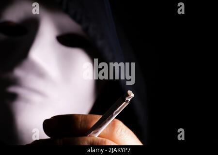 masked man smoking cigarette on dark background Stock Photo - Alamy